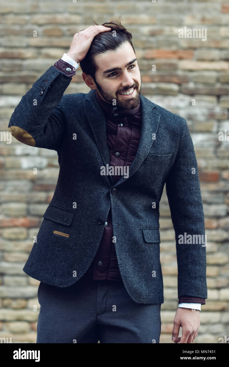 Young bearded man, model of fashion, smiling in urban background wearing british elegant suit ...