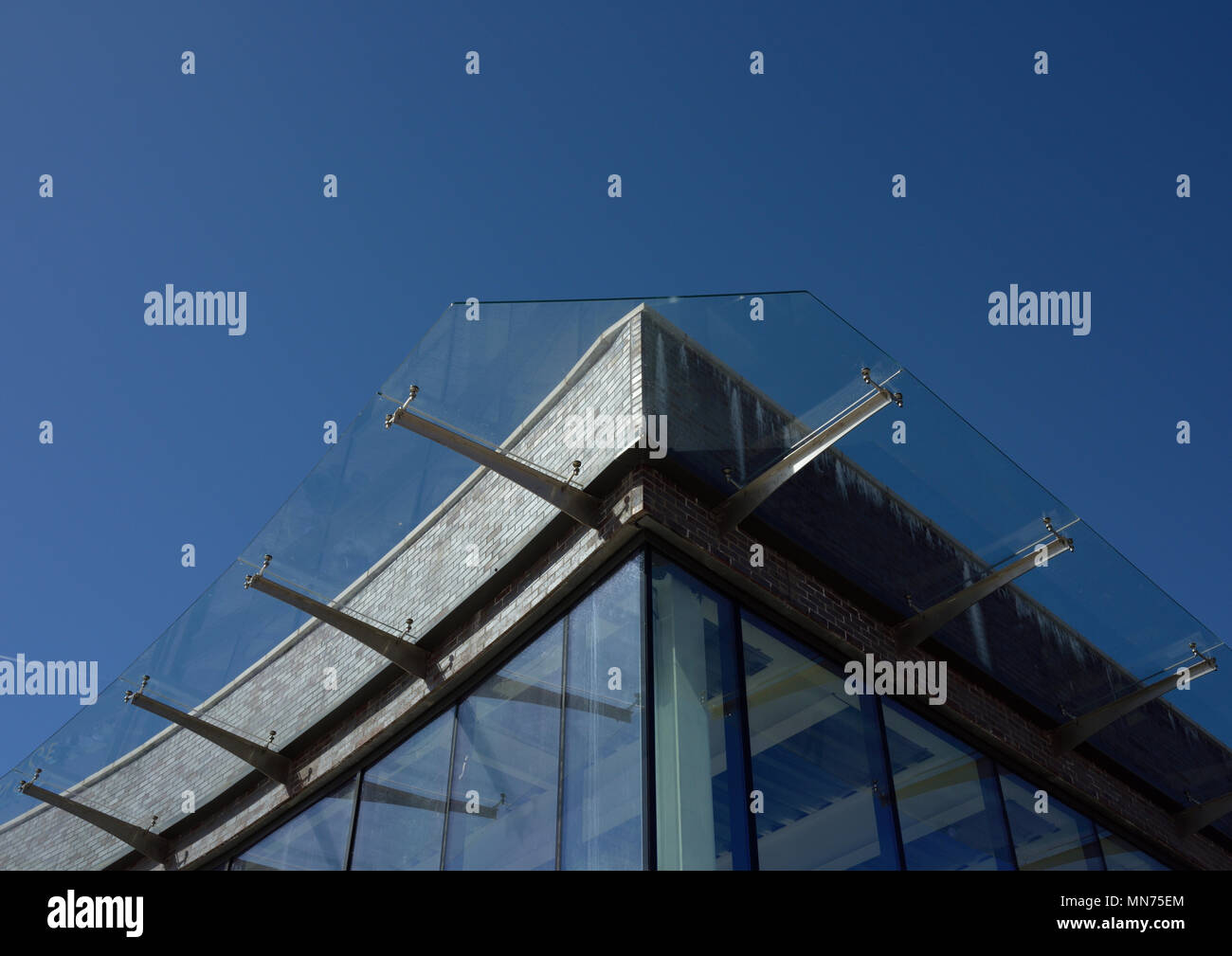 Glass canopy suspended on stainless steel brackets above glass curtain ...