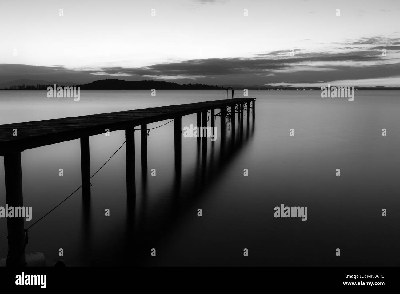 Long exposure view of a pier on a lake at dusk, with distant colorful ...
