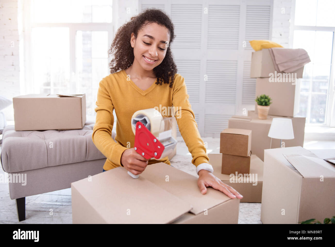 Cheerful curly-haired girl closing box with adhesive tape Stock Photo ...