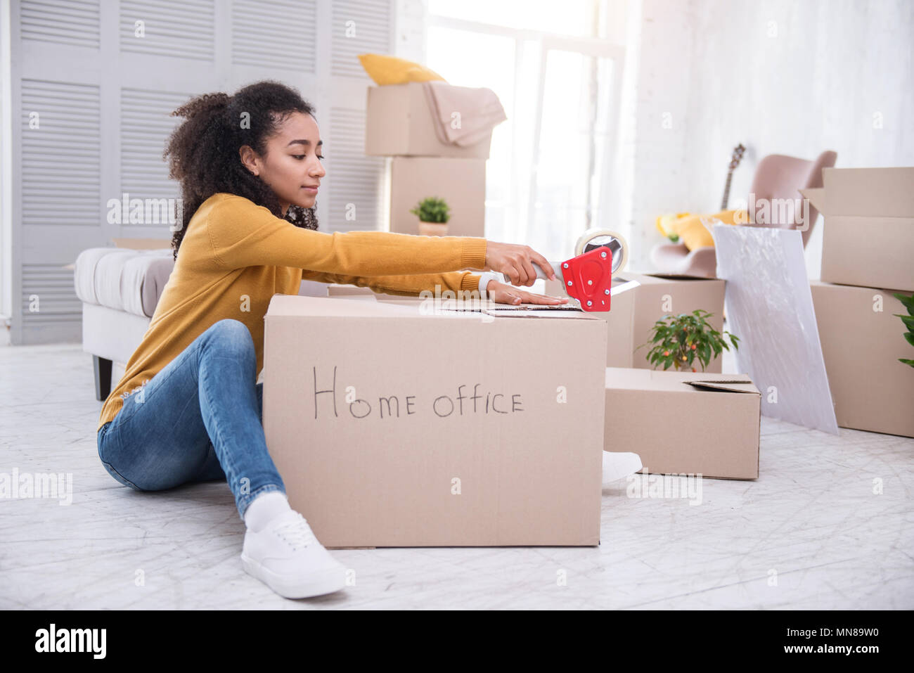 Pleasant girl closing box with office belongings with adhesive tape ...