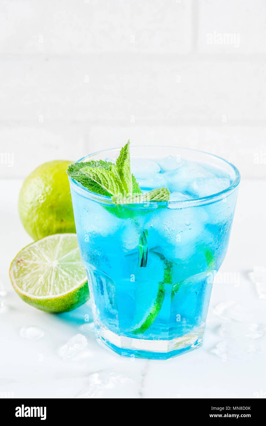 Colorful summer beverage, iced blue lagoon alcohol cocktail drink with lime and mint, white ...