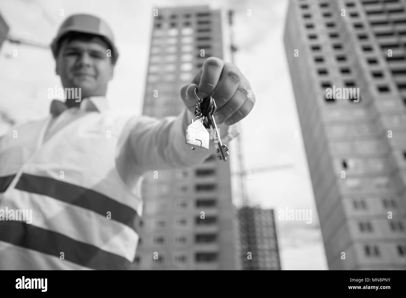 Closeup black and white image of smiling engineer showing keys from new ...