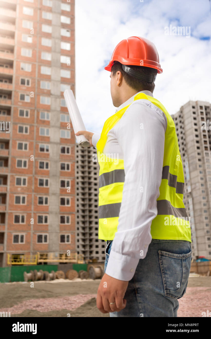 Male construction engineer pointing with blueprints on new house under ...