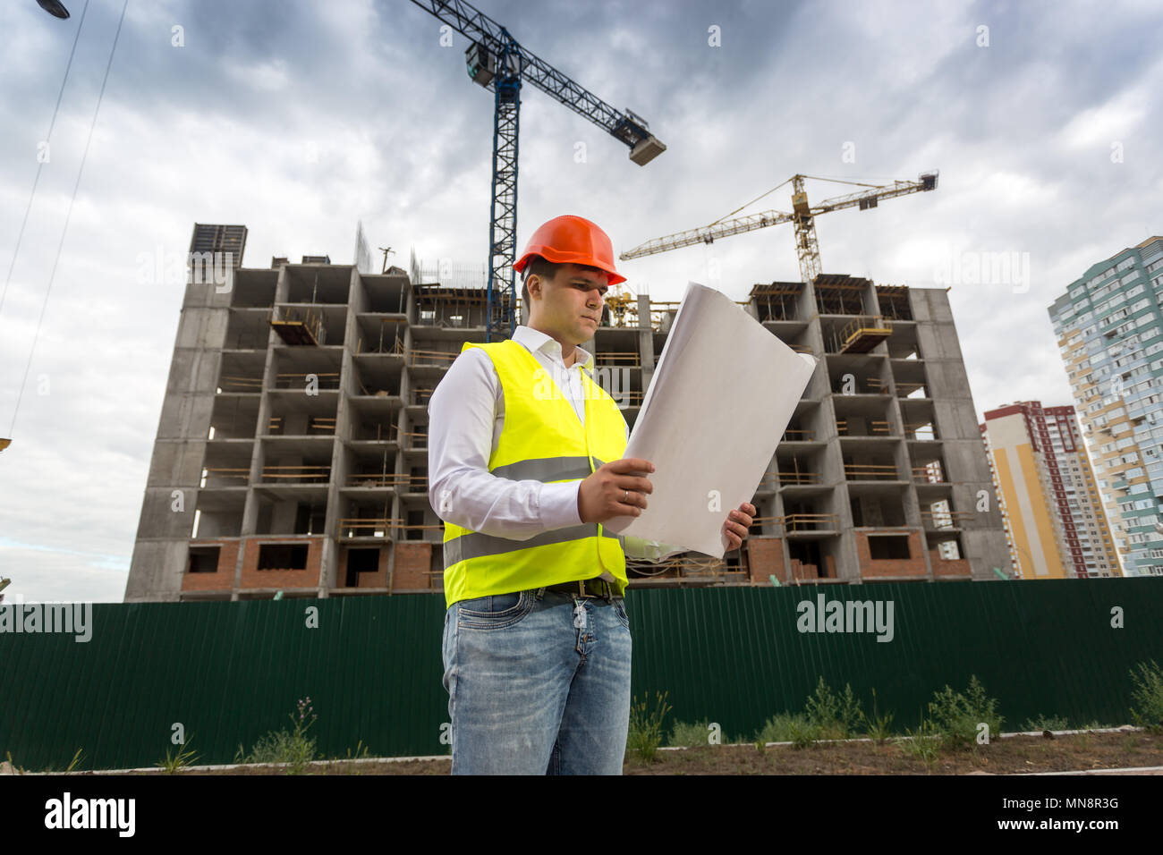 Portrait of construction engineer looking at blueprints on building ...