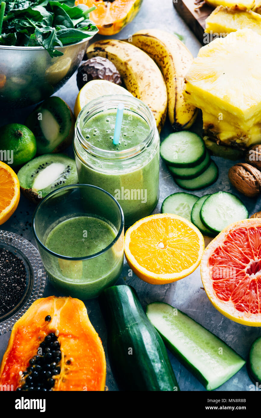 Healthy green detox smoothie drink in a glass surrounded by raw fruit ...