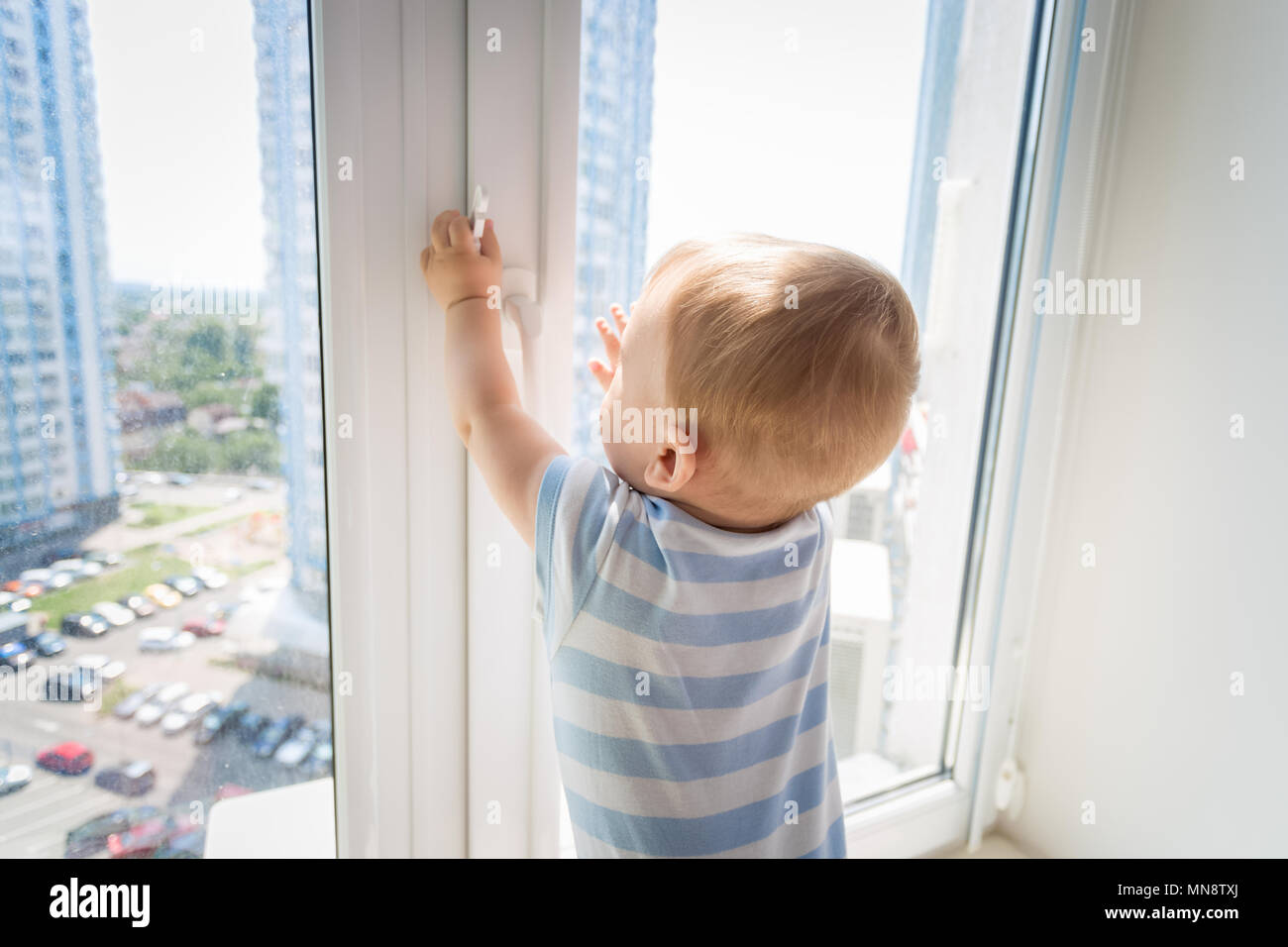 9 months old baby boy standing on windowsill and trying to open the ...