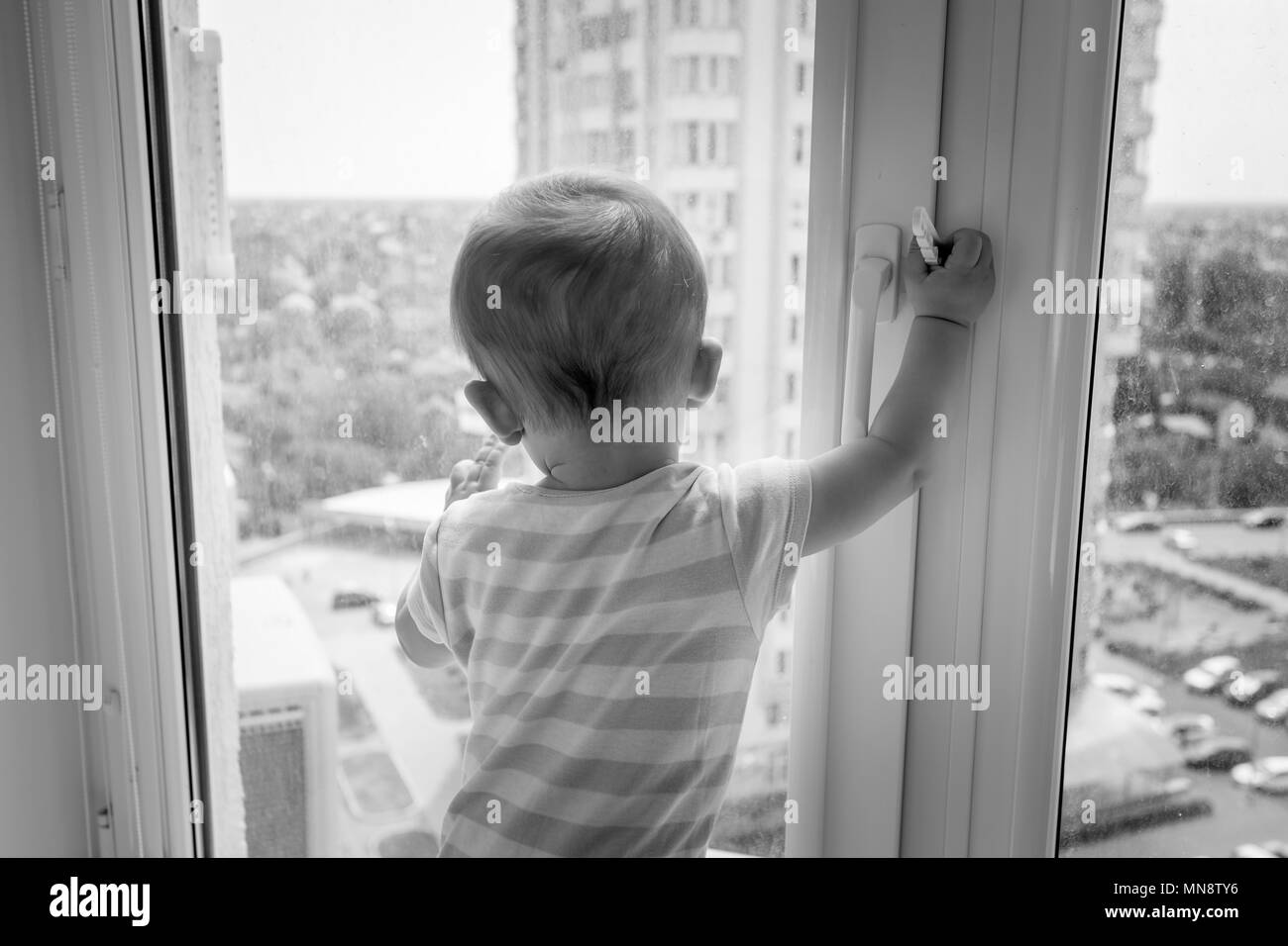 Black and white image of baby pulling window handle and trying to open ...