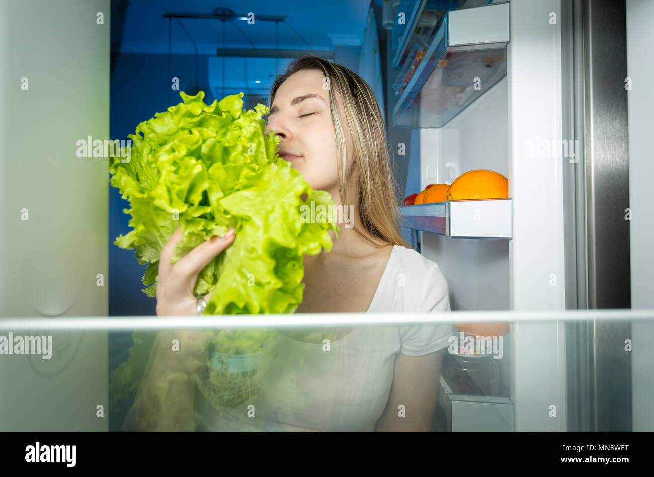 Portrait of young hungry woman looking inside of refrigerator and ...