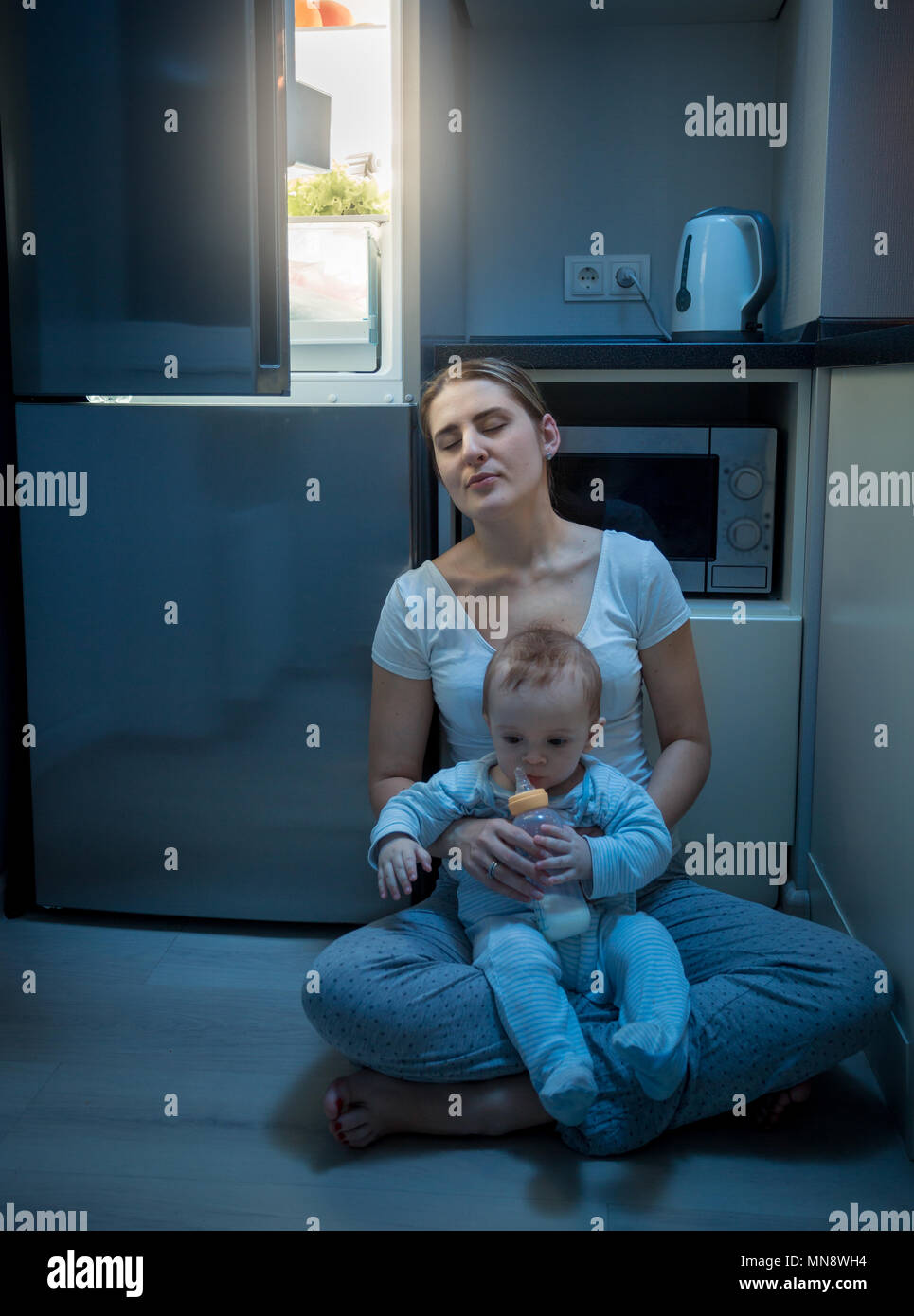 Young mother sleeping on kitchen floor while feeding her baby boy at ...