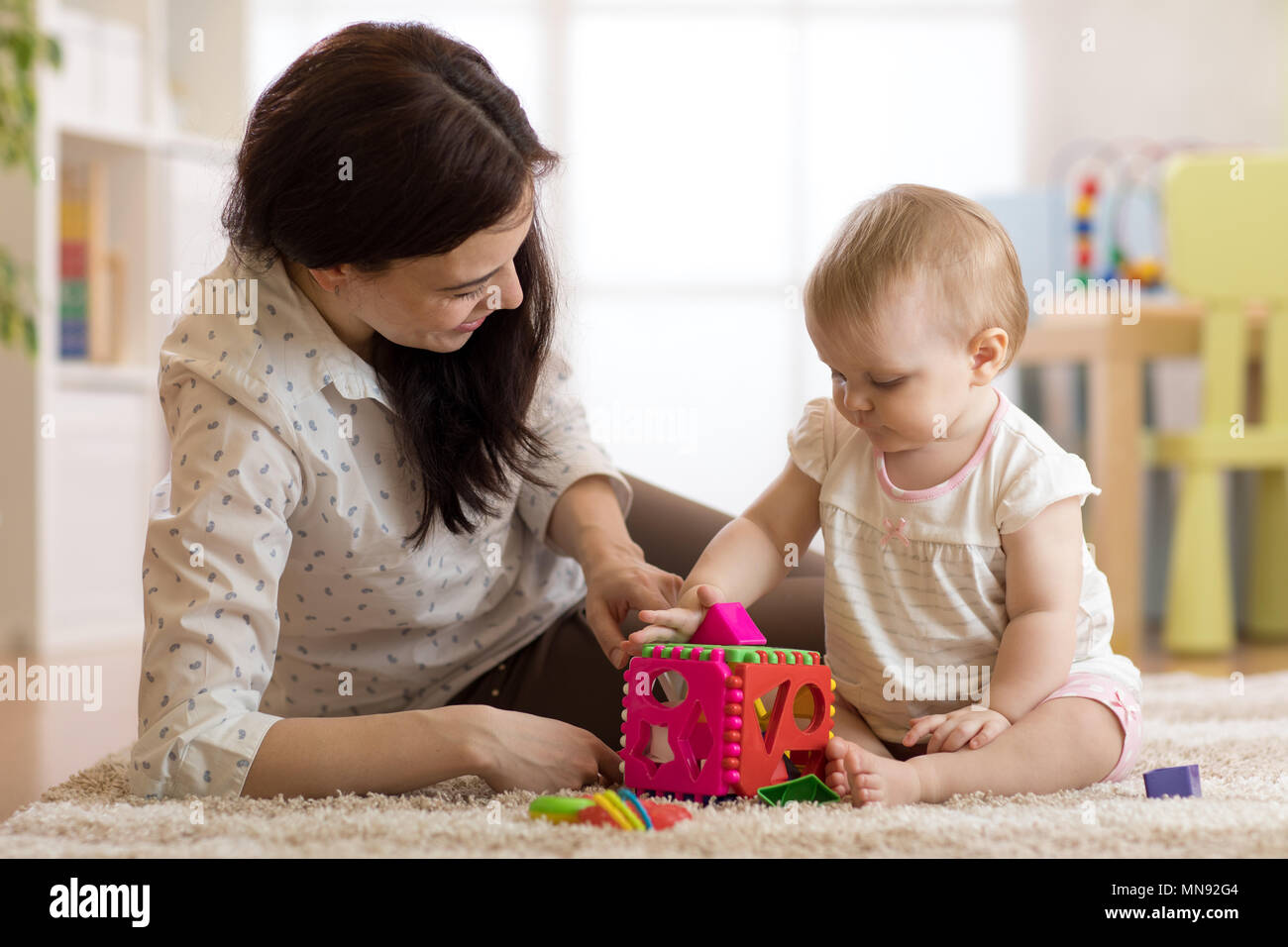 Babysitter looking after baby. Child plays with sorter toy sitting on ...