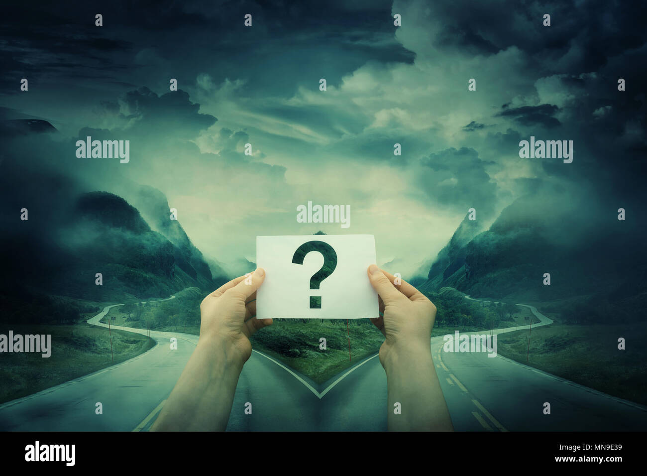 Hands holding a sheet with question mark, in front of a crossroad, fork ...