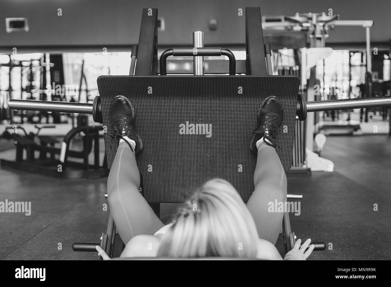 Cute young brunette building leg muscles in a simulator at the gym ...