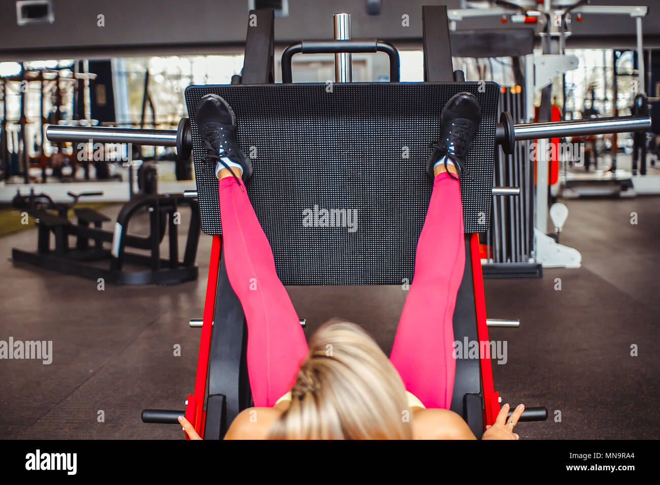 Cute young brunette building leg muscles in a simulator at the gym ...