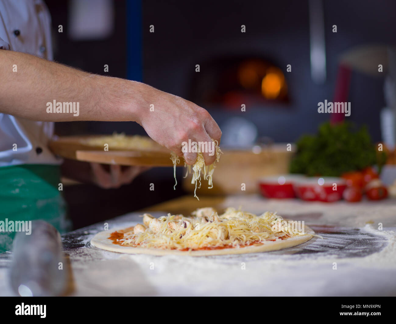 chef sprinkling cheese over fresh pizza dough on kitchen table Stock ...