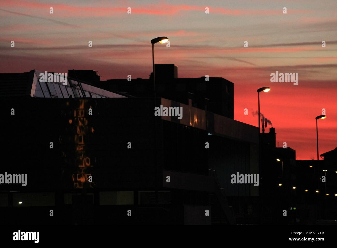 Red glowing sunset over a city street with streetlamps and building ...