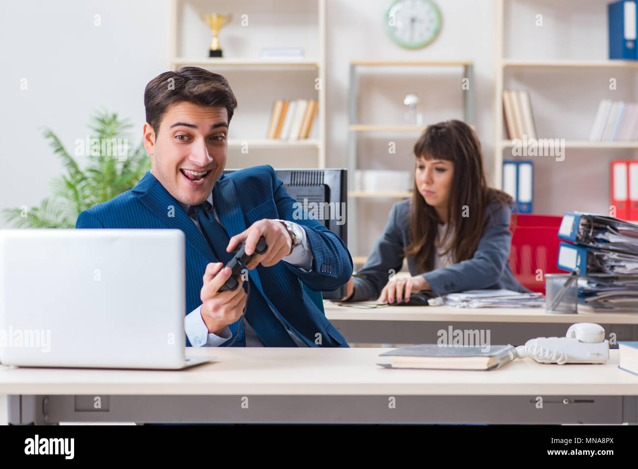 Man playing games in office while colleague is busy Stock Photo - Alamy