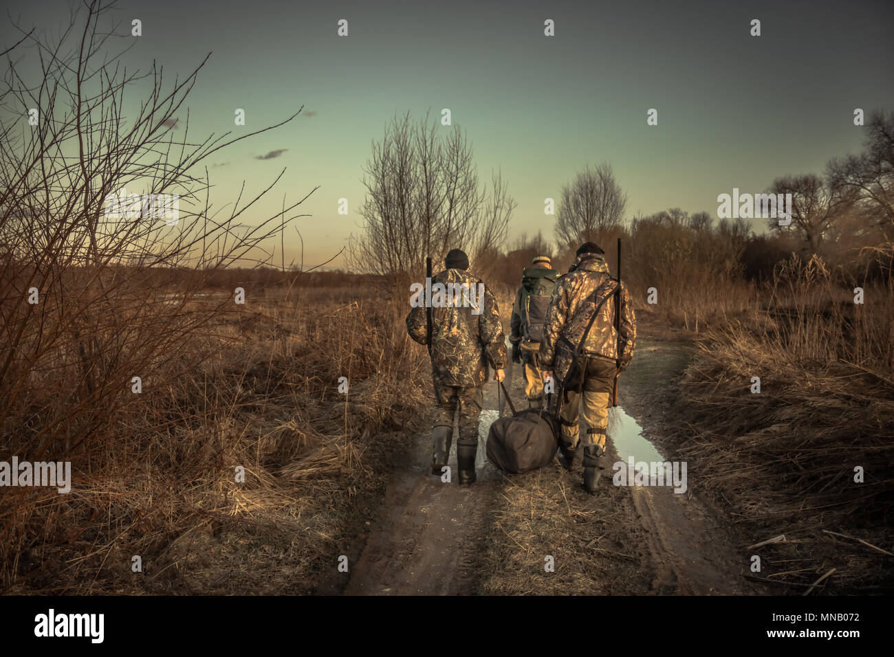 Group of men hunters with hunting equipment walking on country road ...