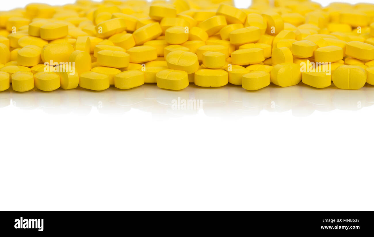 Pile of yellow ovoid-rectangular shape tablet pills isolated on white ...