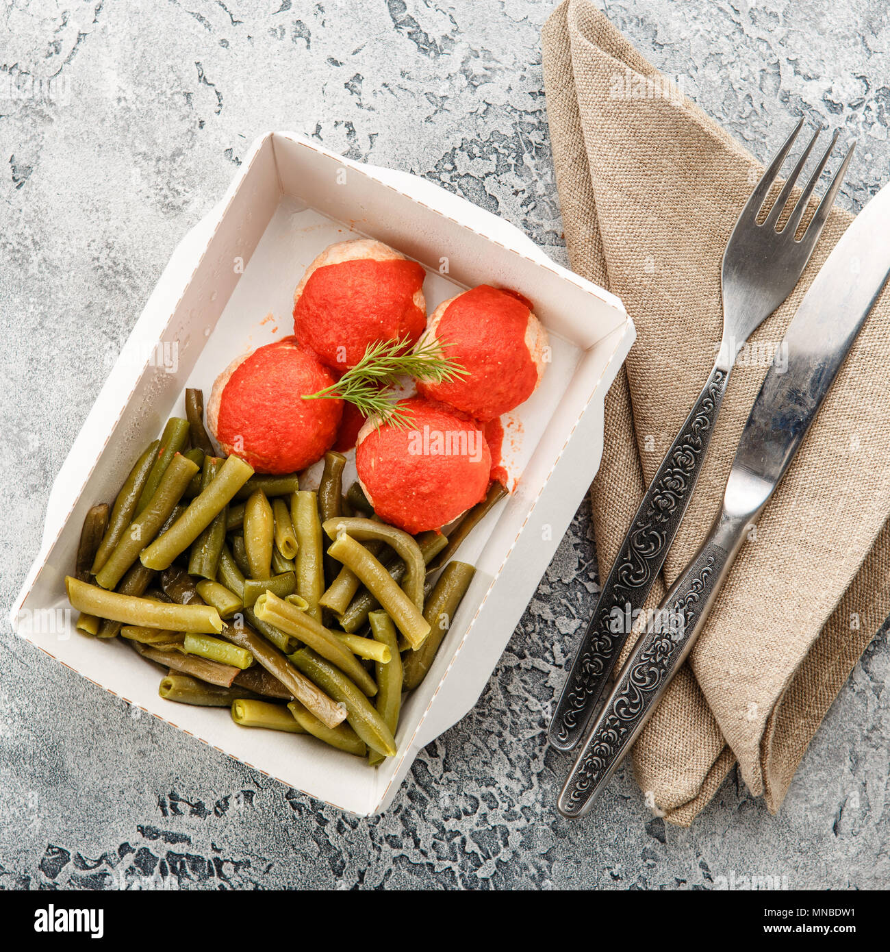 Boiled string beans and fish balls in sauce in a lunchbox on a gray ...