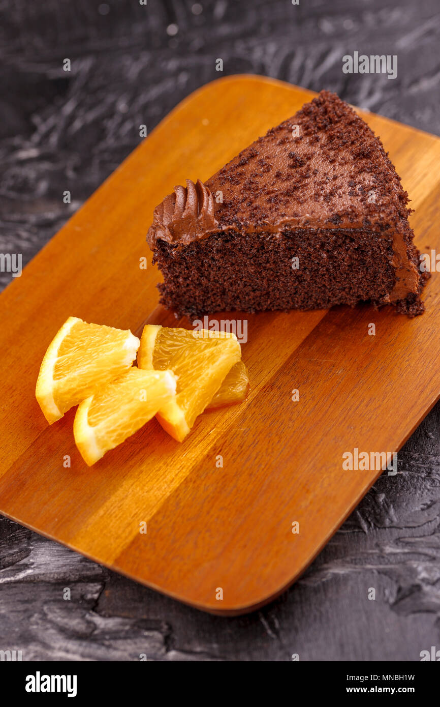 A close up image of rich chocolate cake and orange wedges on a board ...