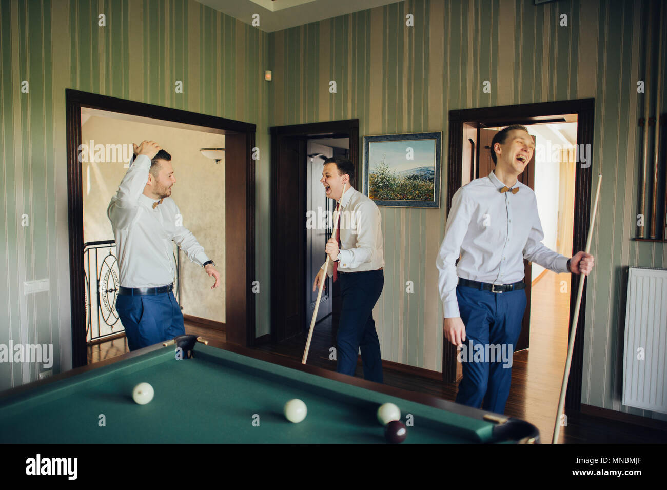 Stylish groomsmen and happy groom playing billiard in the morning for ...