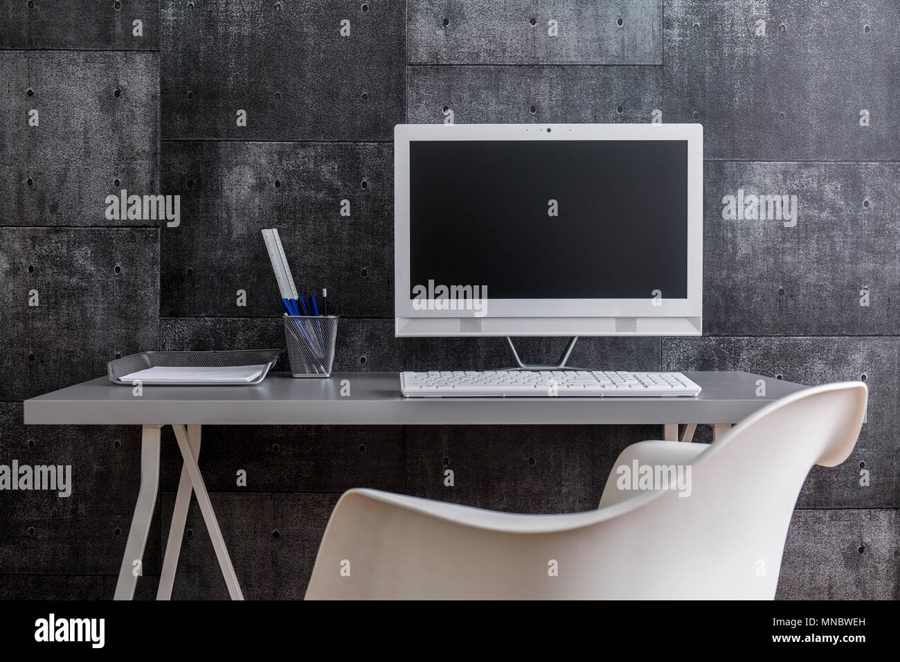 Shot of a modern computer desk with accessories standing by the grey ...