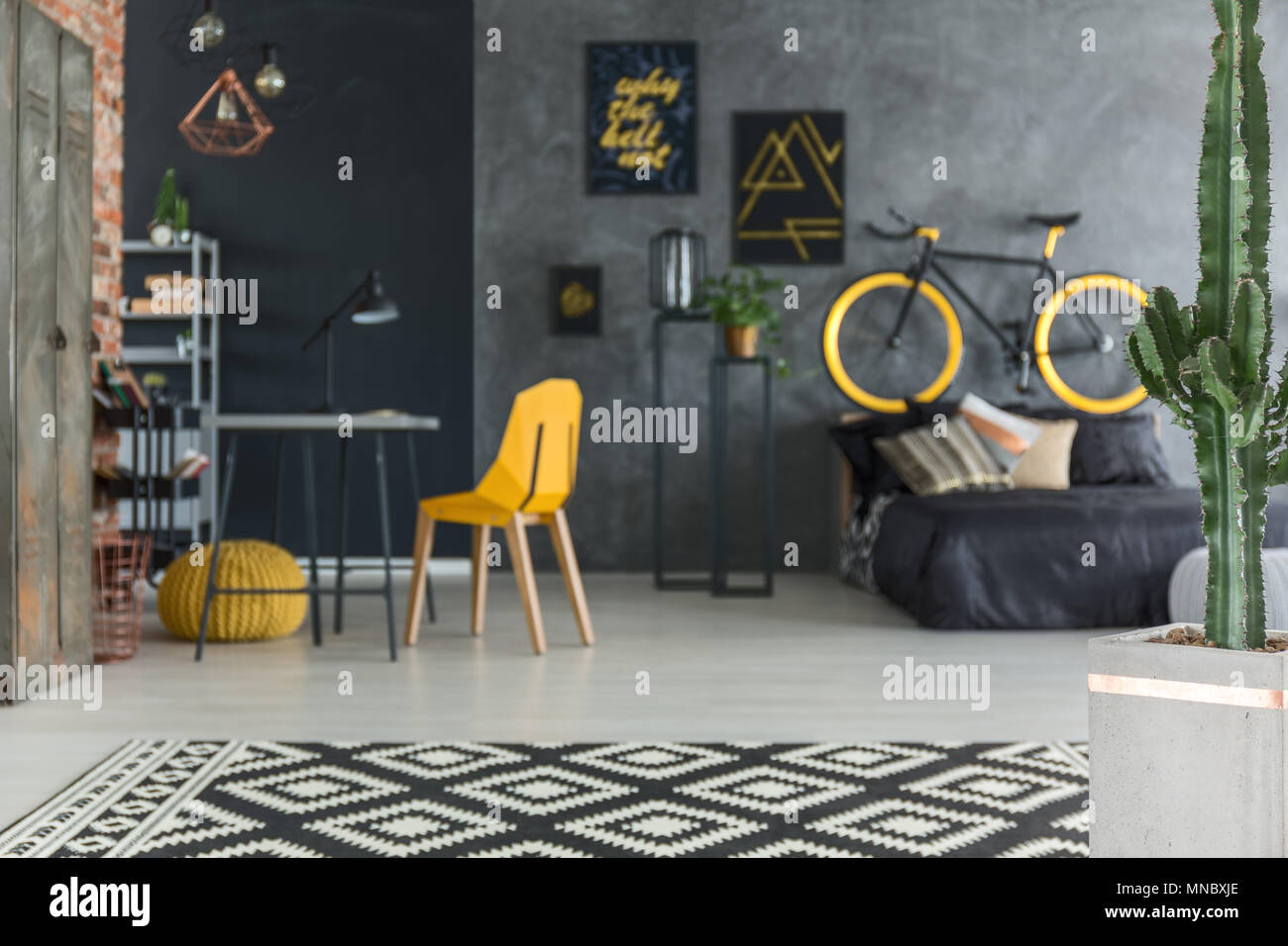 Grey hipster room with bed, bike, yellow chair and desk Stock Photo - Alamy