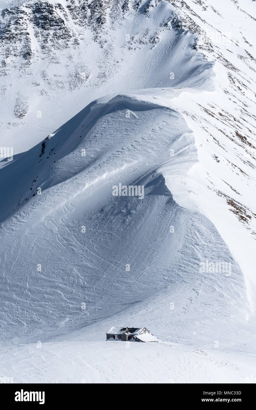 Mountain ridge with large wind packed cornices leaning over partly snow ...