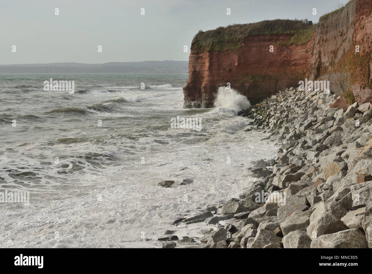Rock armour protecting the base of red sandstone cliffs from rough seas ...