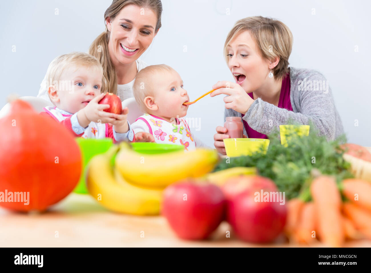 Two happy mothers and best friends smiling while feeding their babies ...