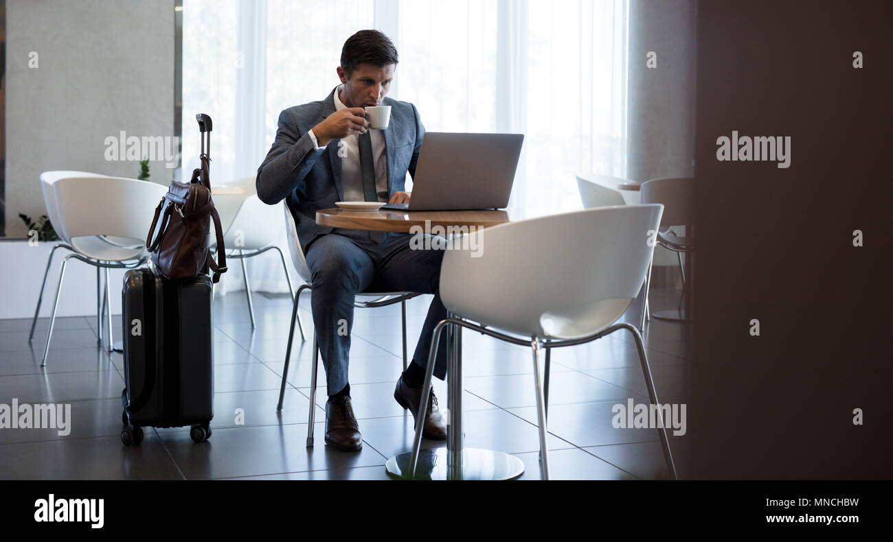 Businessman sitting airport terminal cafe using laptop and drinking ... Businessman sitting airport terminal cafe using laptop and drinking ...