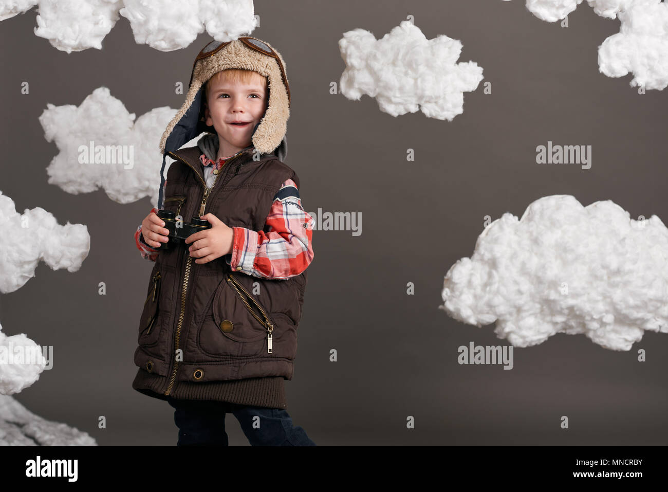 boy dressed as an airplane pilot stands between the clouds and looks ...
