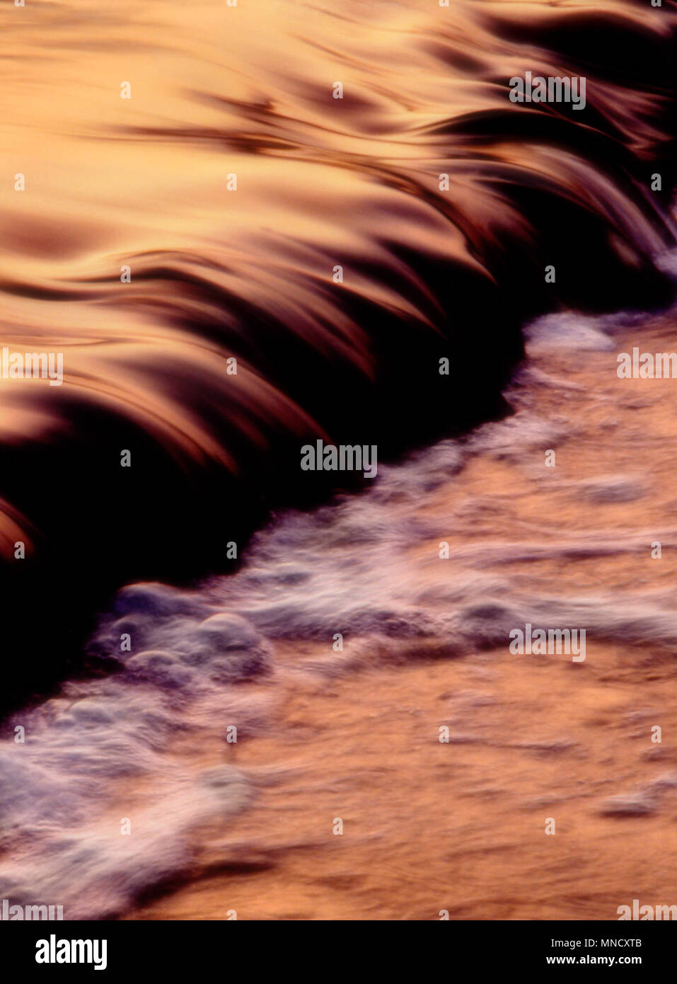 Water flows gently over a shallow crevice under the light of the sunset ...