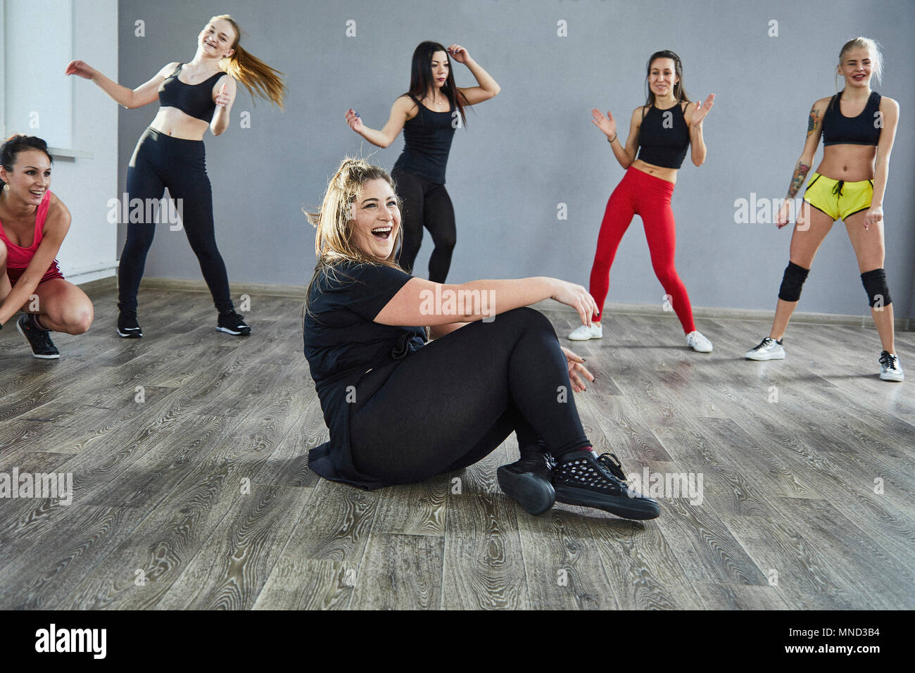 Laughing woman sitting on floor while dancing with friends at studio ...