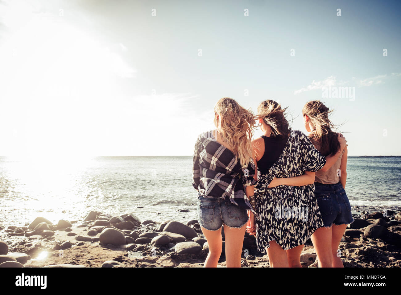 Group of three young nice girls embrace themselves looking at the ocean ...