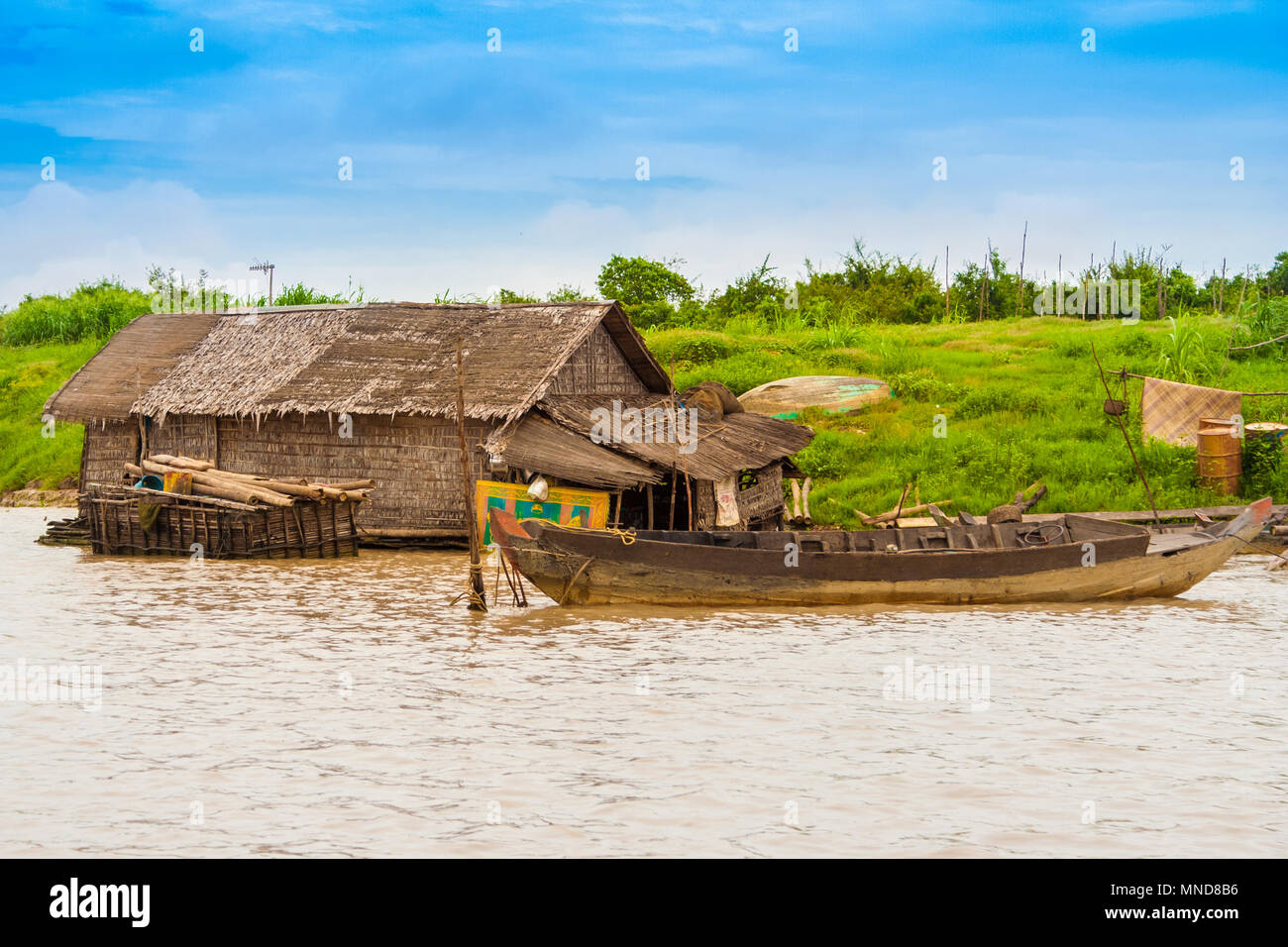 A floating house made of wood and thatch with a tied up wooden boat ...