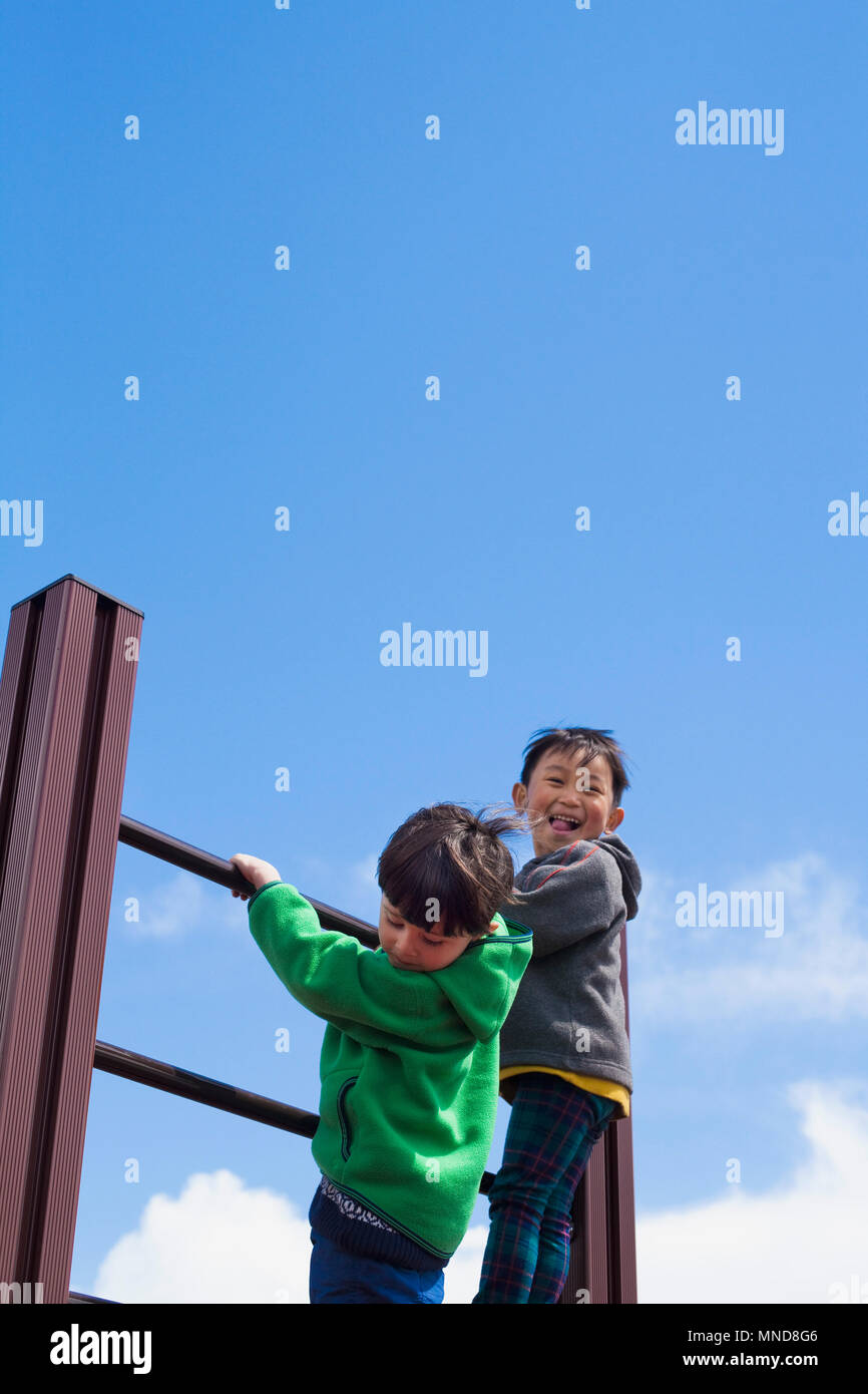 Low angle view of boys climbing on playground equipment against blue ...