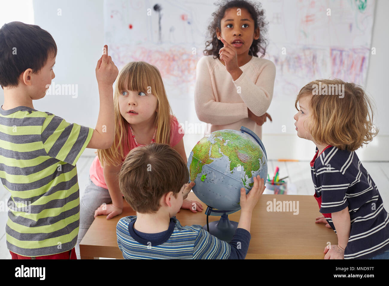Children discussing while exploring globe at table in preschool Stock ...