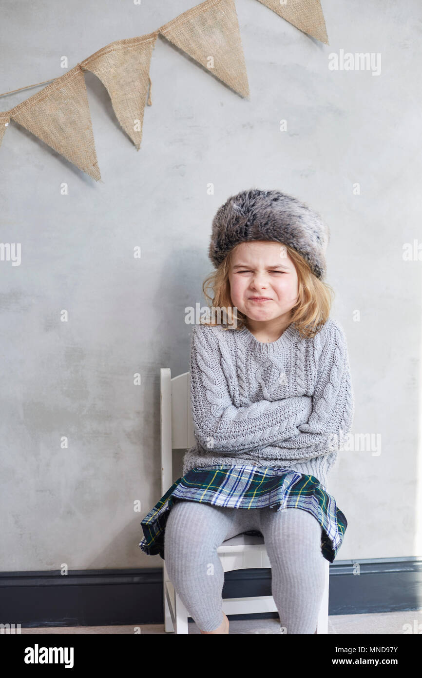 Girl making face while sitting on chair against gray wall Stock Photo ...