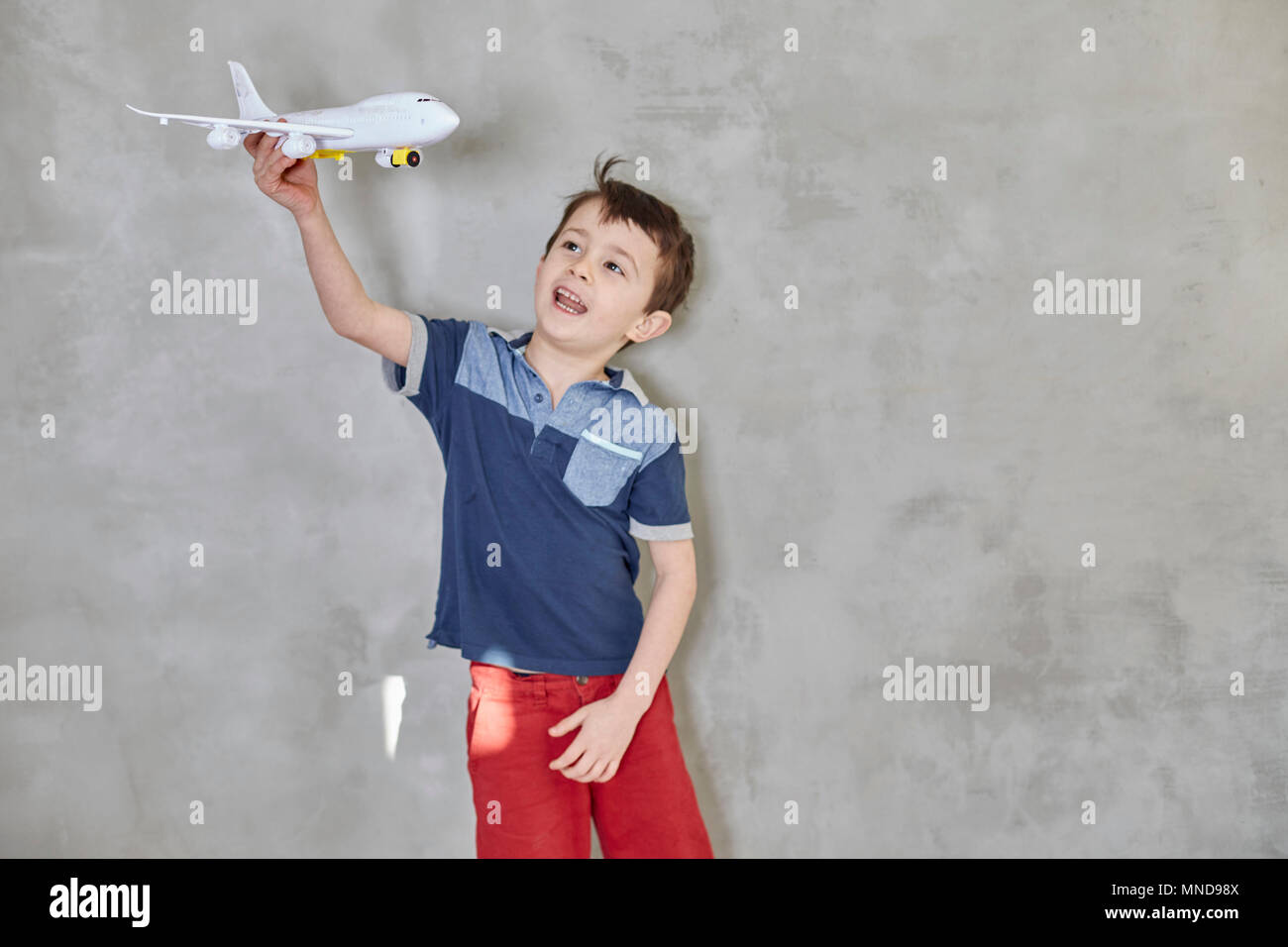 Boy playing with model airplane while standing against gray wall Stock ...