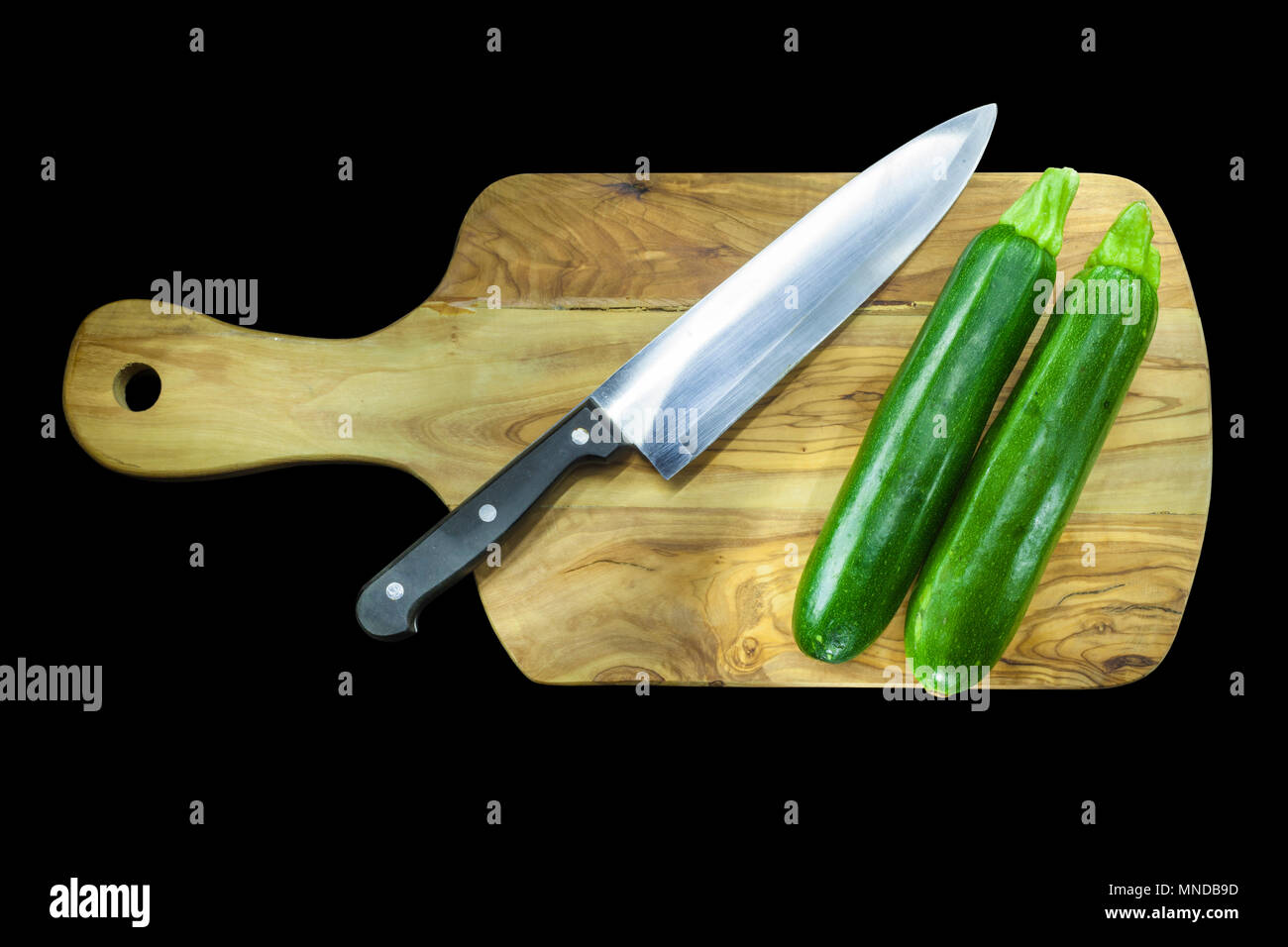 Chopping board with a knife and two courgettes isolated on a black ...