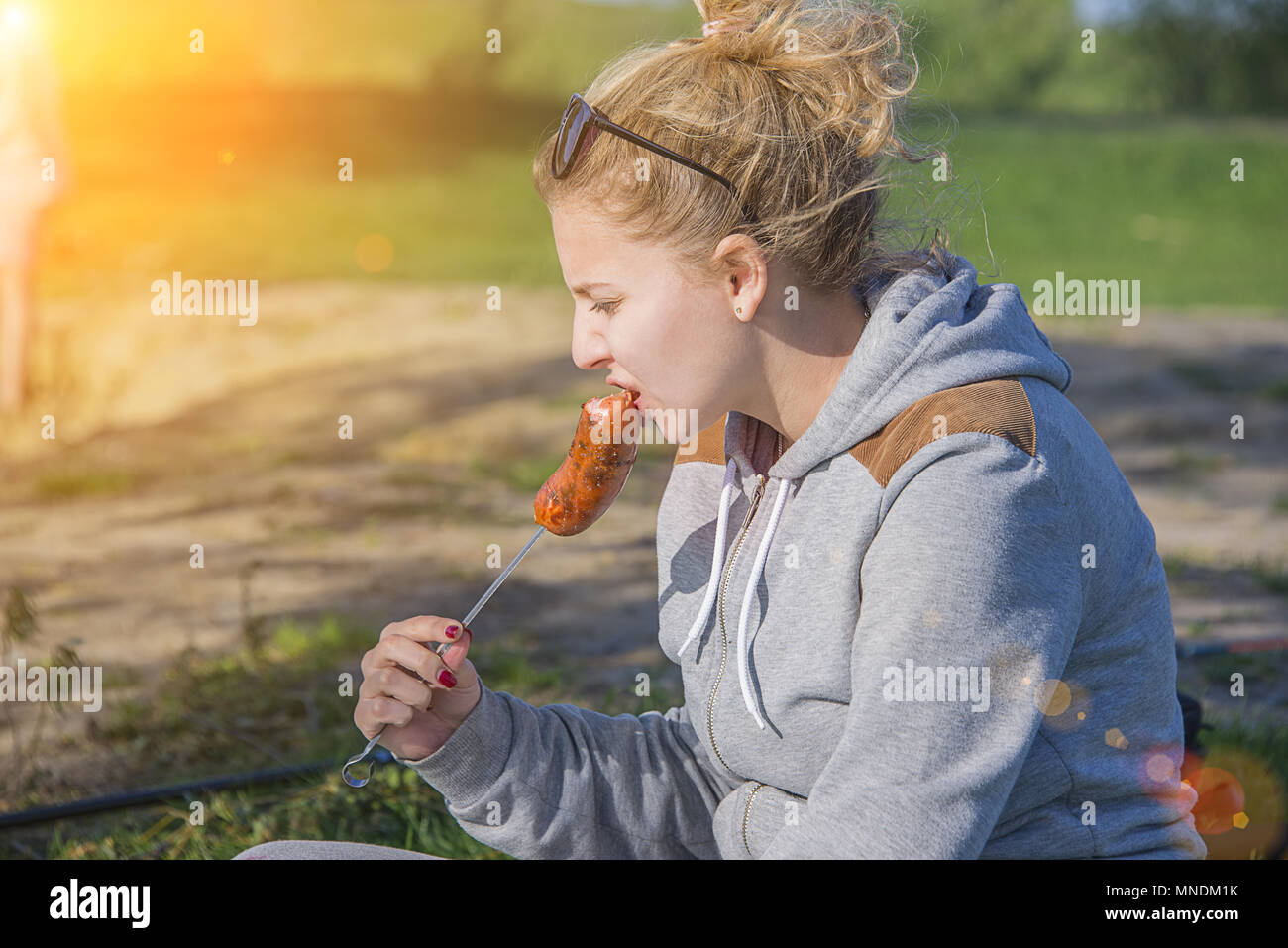 girl eating sausage from the grill, outdoors on the green grass camping ...