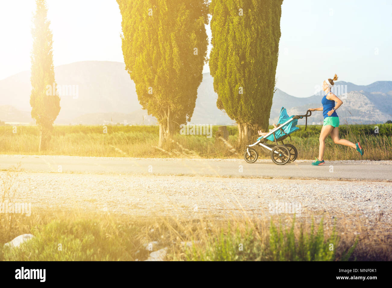 Running mother with child in stroller enjoying motherhood at sunset and ...