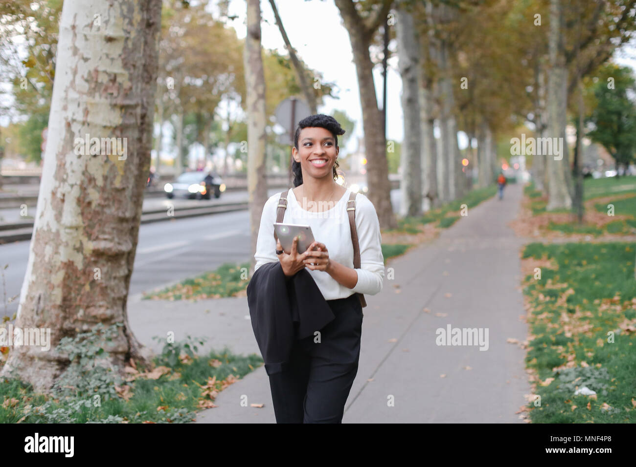 Black female pretty student using tablet and walking on street with ...