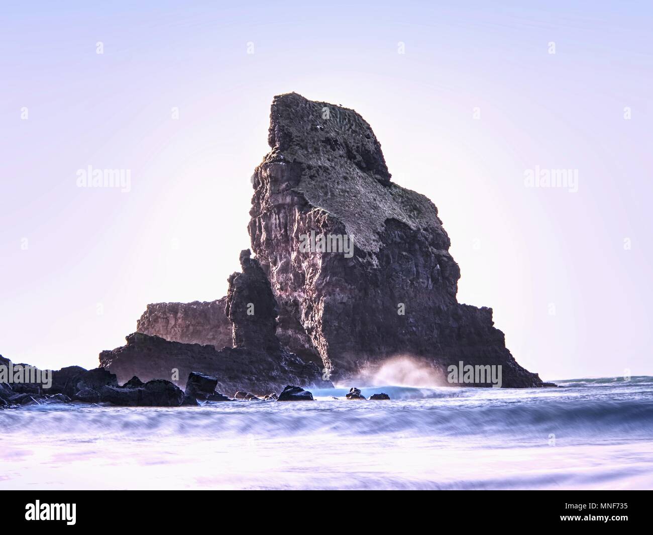 Sea stack sharp silhouette by sunset sky. Evening light on the rocks ...