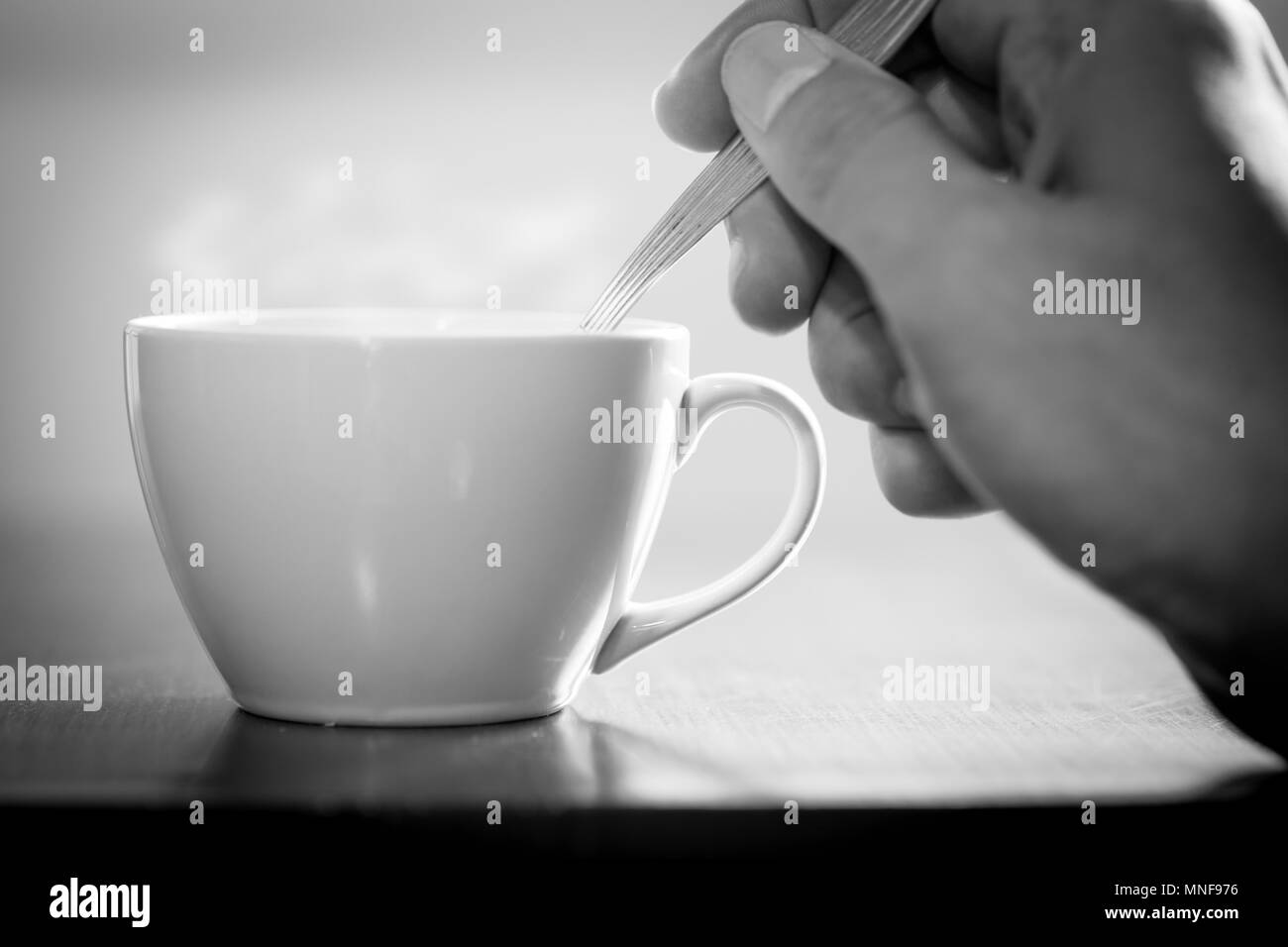 One using spoon mixing hot coffee with sugar and cream. Monotone effect ...