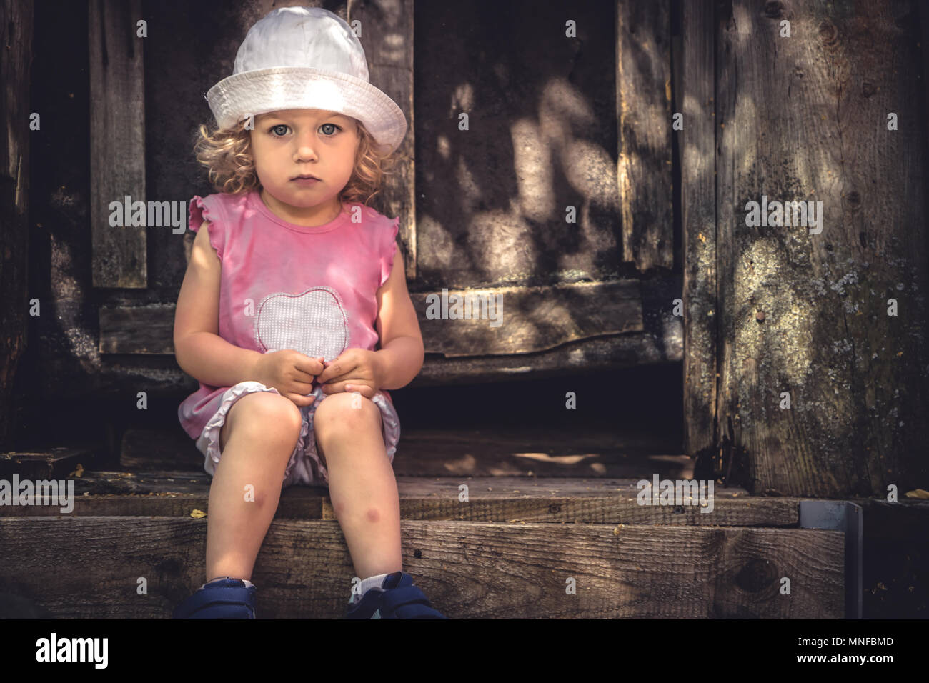 Sad lonely child girl upset look sitting lonely on door steps old house ...