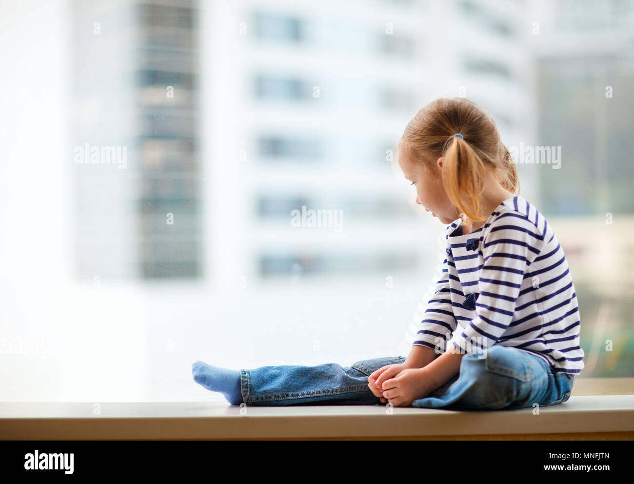 Adorable little girl sitting by the window Stock Photo - Alamy