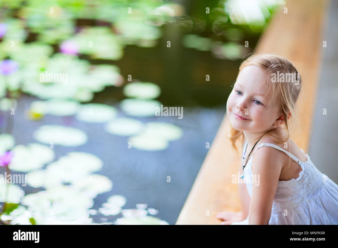 Adorable little girl sitting near water lily pond Stock Photo - Alamy